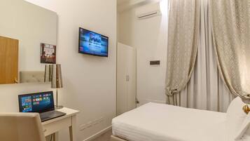 Quarto de hotel com cama, secretária com laptop, televisão na parede e guarda-roupa.