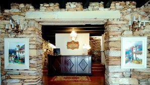Um arco de pedra que dá acesso a um saguão com uma escada de madeira, um balcão de recepção e obras de arte emolduradas nas paredes.