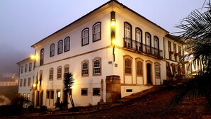 Um edifício grande e histórico com várias janelas e uma varanda, rodeado por um pavimento de calçada.