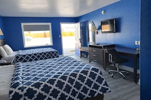 Quarto de hotel com duas camas, uma escrivaninha, uma cadeira, uma TV e vista para um parque de estacionamento.