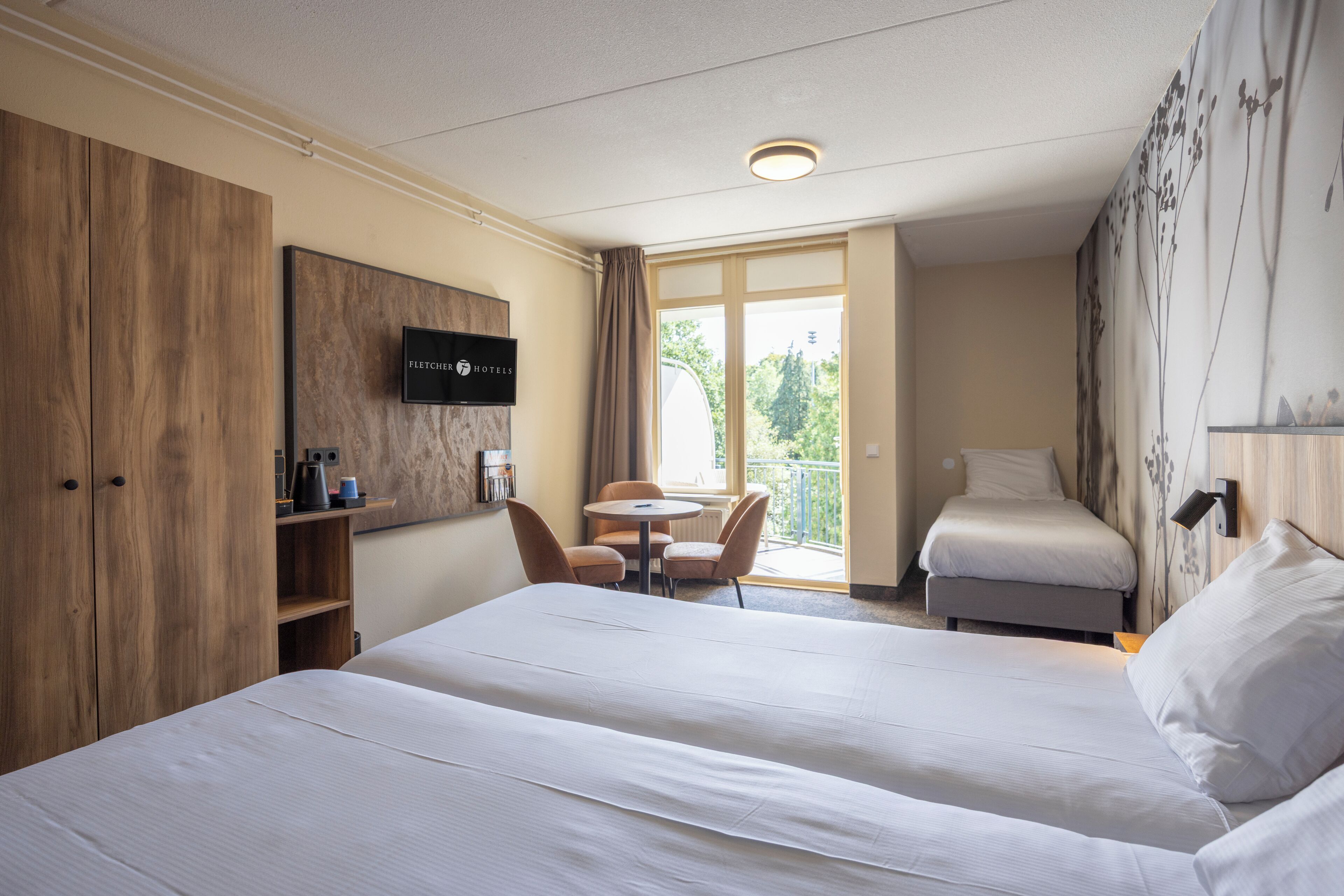 Quarto de hotel com cama, escrivaninha, cadeira, televisão e varanda com vista.