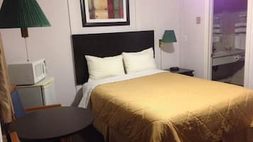 Quarto de hotel com uma cama, uma mesa, uma cadeira, micro-ondas, abajur e um quadro na parede.
