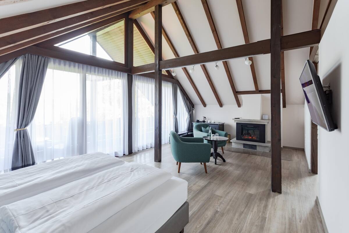 Quarto de hotel com uma cama grande, lareira, televisão e área de refeições com cadeiras.