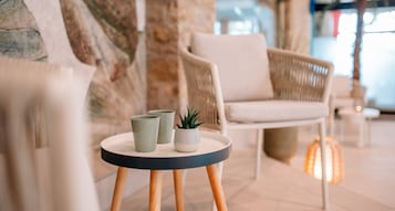 Uma mesa redonda com três chávenas de cerâmica e uma pequena planta num vaso. Uma cadeira de vime está ao fundo.