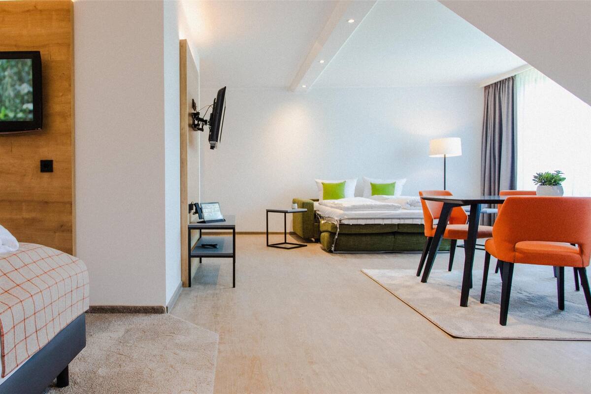 Quarto de hotel com cama, escrivaninha, cadeira, televisão e janela.
