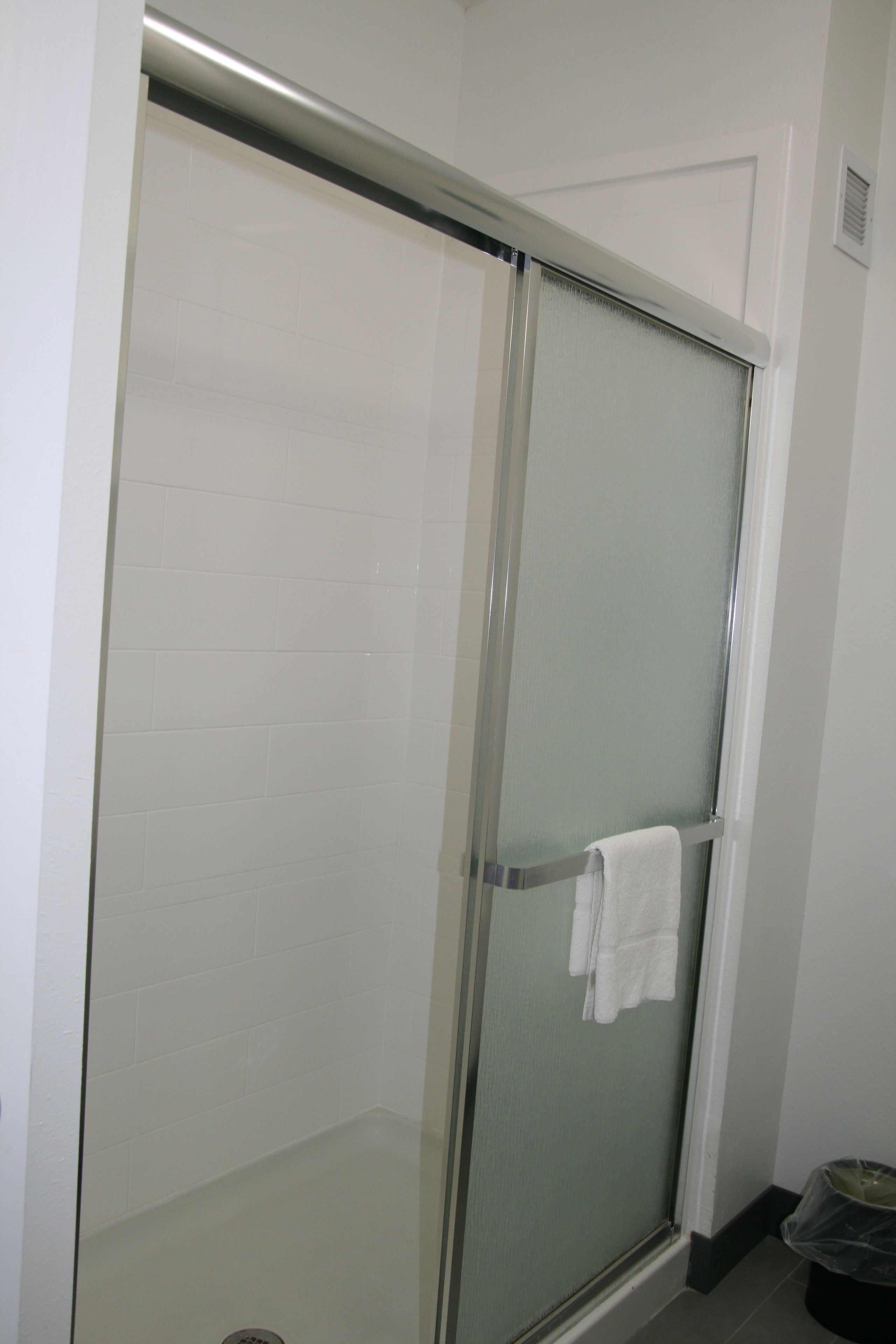 Divisória de chuveiro com paredes de vidro e uma toalha branca pendurada no puxador da porta.