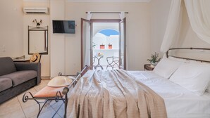Quarto com cama, sofá, televisão, varanda com vista e ventoinha no teto.