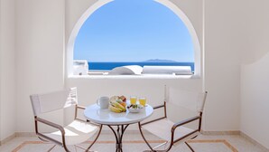 Uma área de refeições com mesa posta para o café da manhã, janela com vista para o mar e interior em tons de branco.