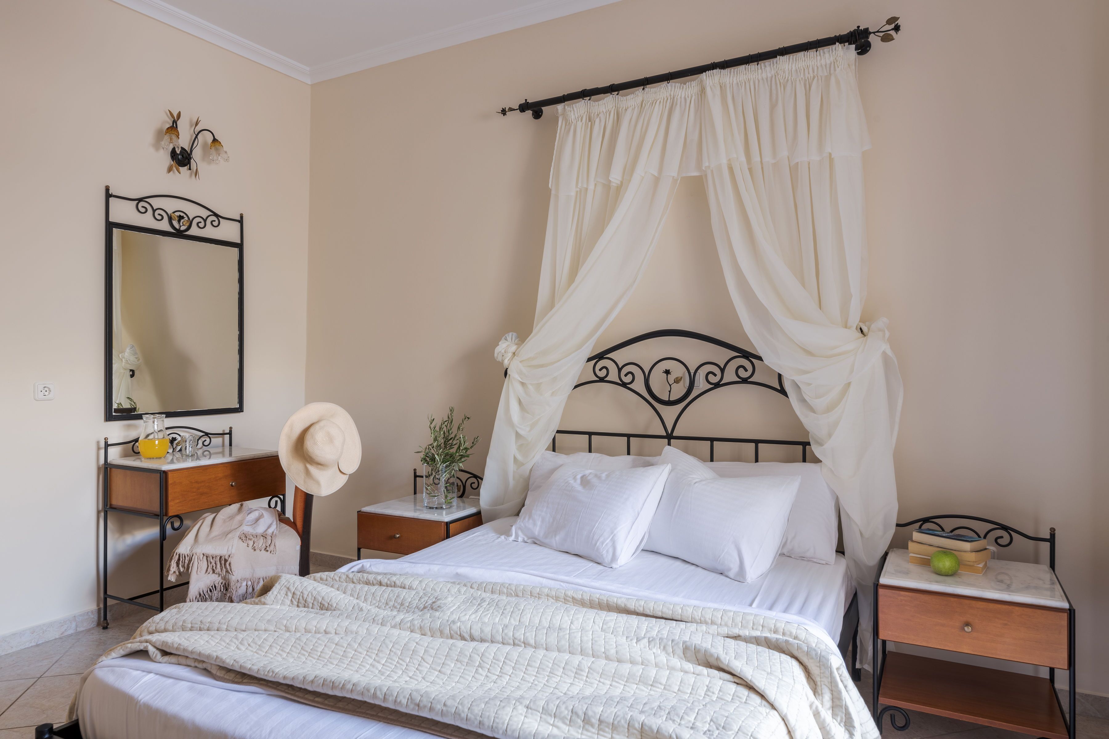 Um quarto bem arrumado com uma cama de dossel, uma mesa de cabeceira com abajur e um espelho na parede.