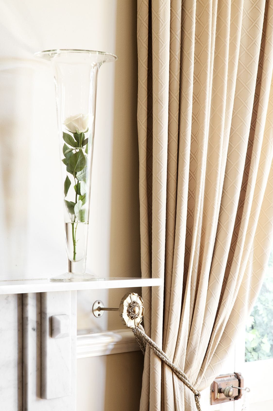 Um quarto com uma prateleira branca que contém um vaso transparente com uma rosa branca e uma chave.
