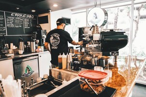 Interior de uma cafeteria com um barista preparando bebidas no balcão.