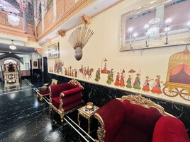 Um lobby luxuoso com decorações elaboradas nas paredes, um lustre imponente e assentos vermelhos macios.