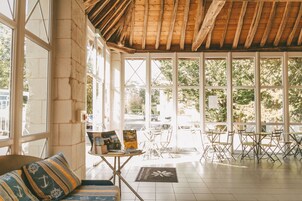 Um quarto espaçoso com grandes janelas, teto de madeira e um espaço de estar com sofá e mesas.