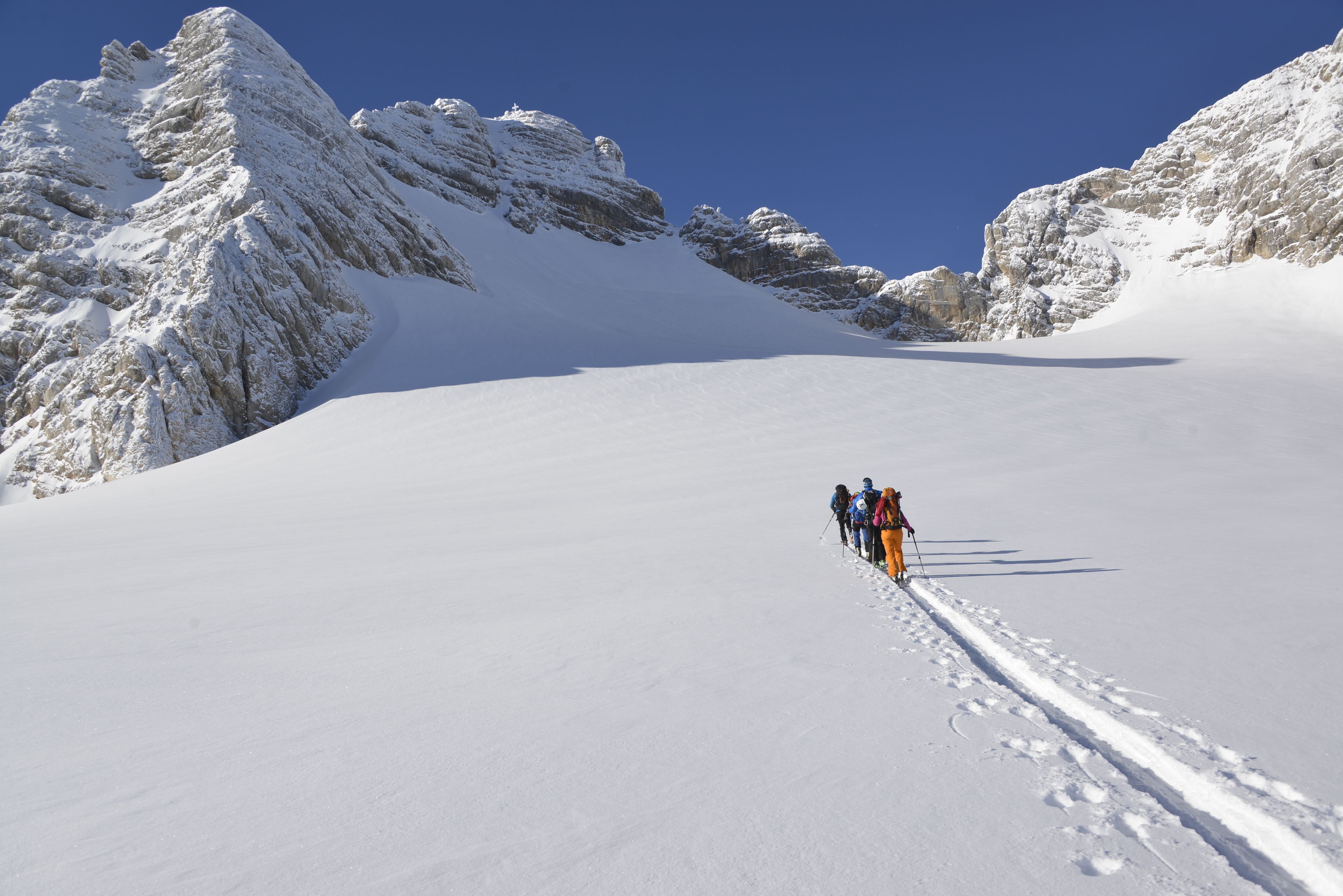 Uma trilha nevada na montanha com um grupo de pessoas caminhando.