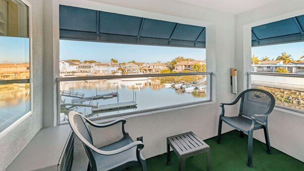 Varanda com duas cadeiras e uma mesa pequena, com vista para uma marina com barcos e casas.