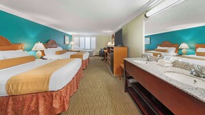 Quarto de hotel com duas camas, uma escrivaninha, um espelho grande e banheiro com pia e bancada.