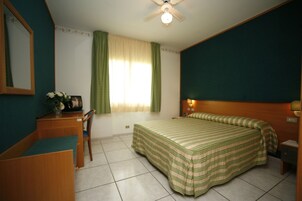 Quarto com cama, escrivaninha, cadeira, mesa de cabeceira e ventilador de teto.