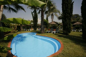 Piscina cercada por espreguiçadeiras e palmeiras.