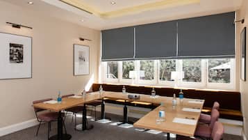 Uma sala de conferências com uma mesa comprida, cadeiras, um projetor e um grande janelão com persianas.