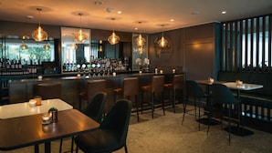 Uma área de bar com várias opções de assento, um balcão de bar com diversos tipos de garrafas e iluminação pendente.