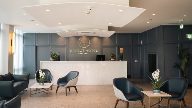 Uma área de recepção de hotel com design moderno, com balcão de atendimento, área de estar e um grande logotipo na parede.