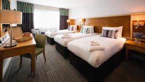 Quarto de hotel com duas camas, uma escrivaninha com abajur, uma cadeira e uma mesinha com uma caixa de pizza.