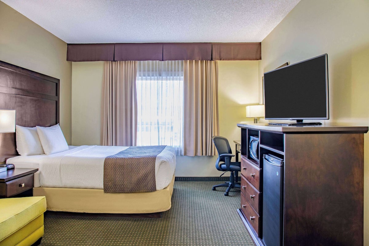 Quarto de hotel com cama, escrivaninha, televisão e uma cadeira.