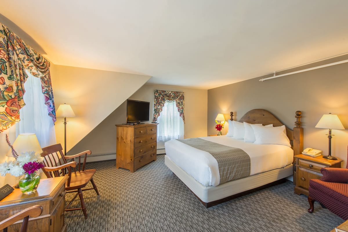Quarto de hotel com uma cama grande, uma escrivaninha com abajur, uma cadeira, um penteado e uma televisão.