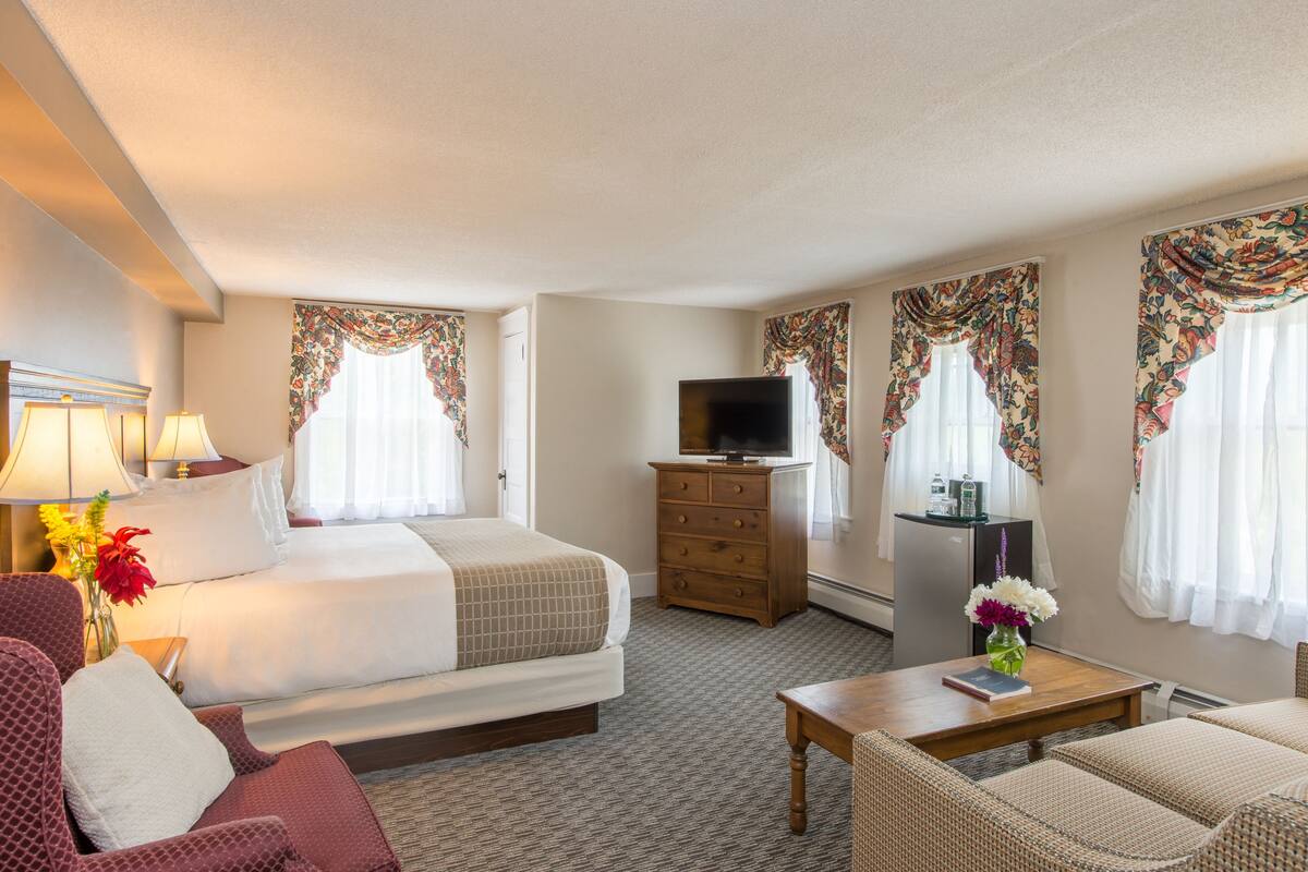 Quarto de hotel com uma cama, televisão, penteadeira, escrivaninha e uma cadeira.