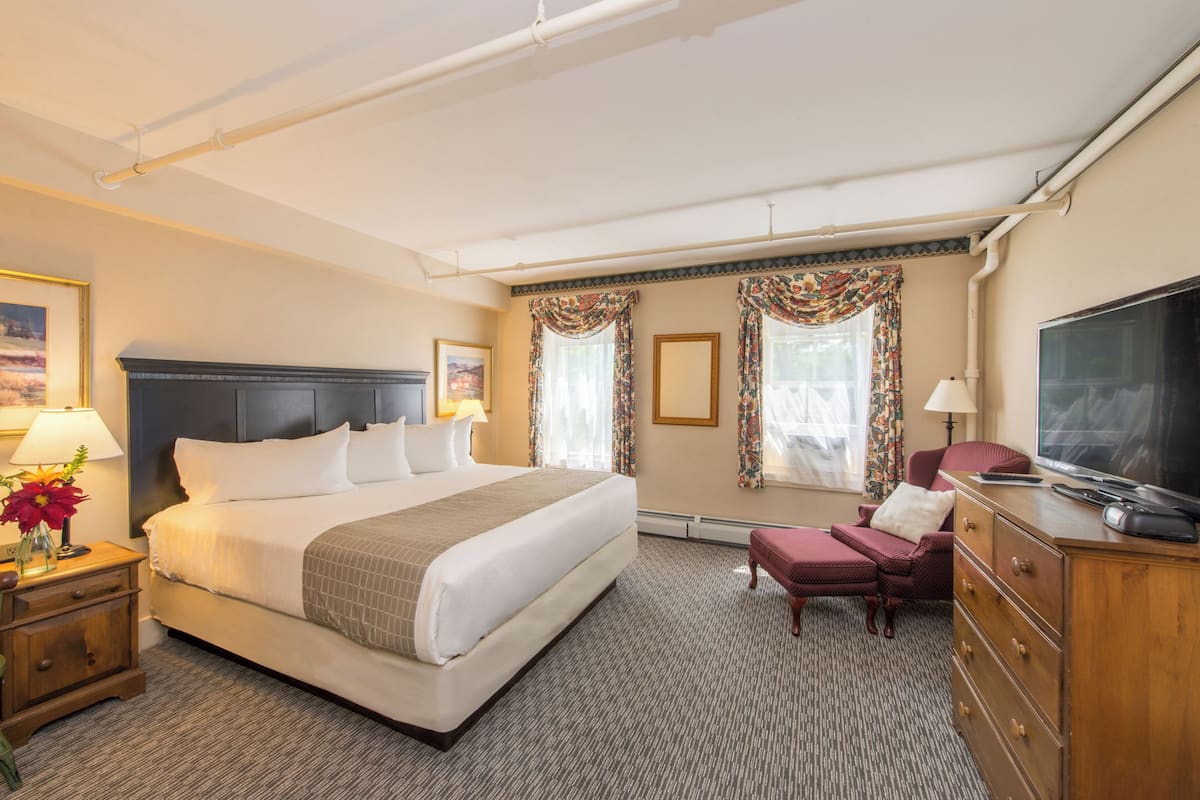 Quarto de hotel com uma cama grande, televisão, escrivaninha com candeeiro e uma cadeira.