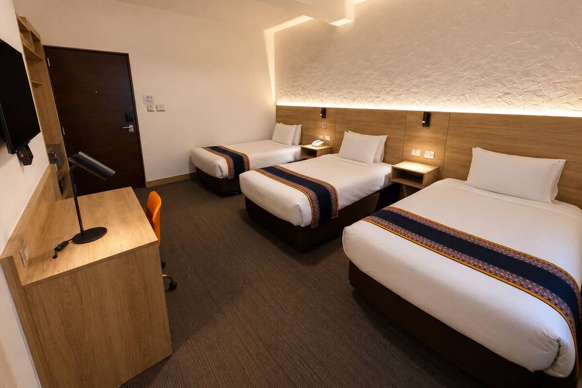 Quarto de hotel com duas camas de solteiro, uma escrivaninha com cadeira e uma televisão.