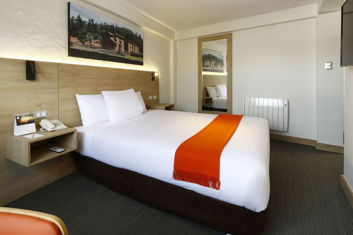 Quarto de hotel com cama, mesa de cabeceira, telefone e espelho.
