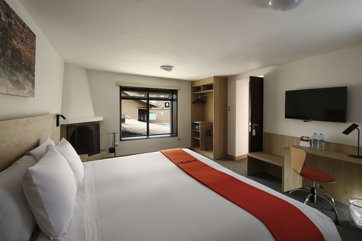 Quarto de hotel com cama, escrivaninha, televisão, janela e cabideiro.