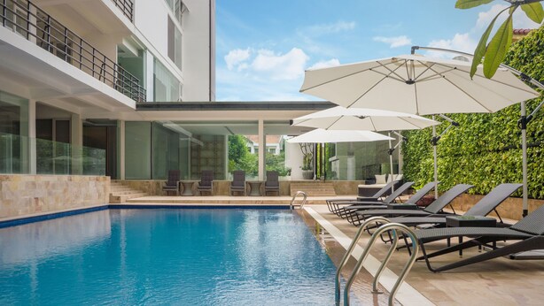 Uma área de piscina moderna, com piscina azul límpida, espreguiçadeiras e guarda-sóis.