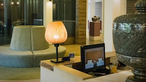 Uma mesa de recepção com uma luminária, um monitor exibindo um quarto e um vaso grande.