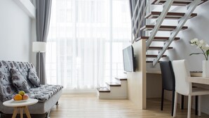Uma sala de estar moderna com sofá, uma mesinha redonda com frutas, televisão e escada.