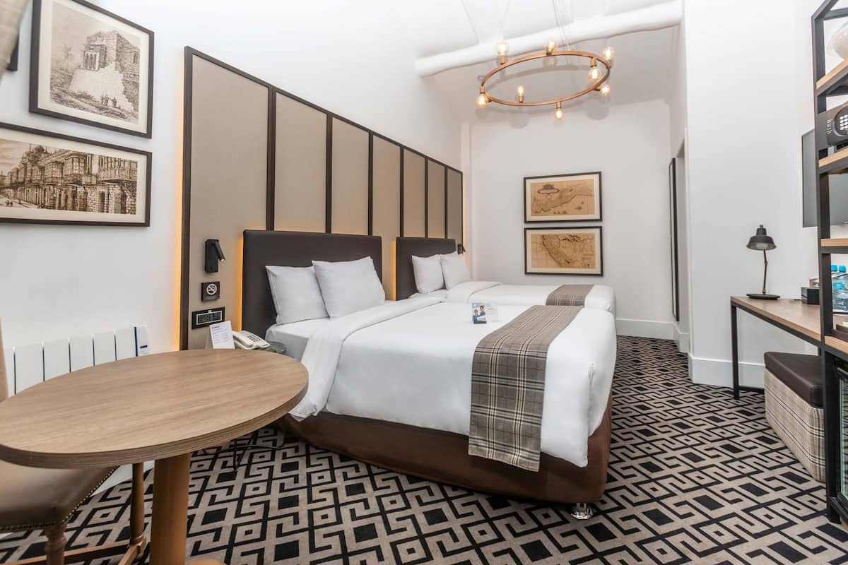 Quarto de hotel com uma cama grande, mesa de cabeceira, escrivaninha e piso estampado.