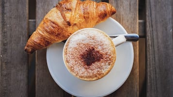 Um croissant e uma xícara de café sobre um prato branco em uma mesa de madeira.