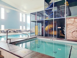 Piscina interna com plataforma de mergulho, área de estar e estrutura de recreação visível através de uma tela de proteção.