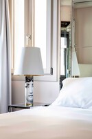 Quarto de hotel com cama, mesa de cabeceira com abajur e janela com cortinas.
