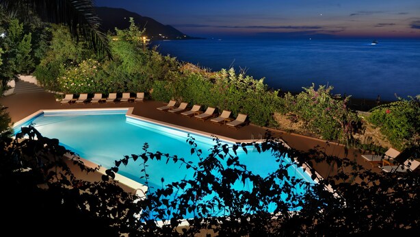 Piscina com espreguiçadeiras e vista para o mar à noite.