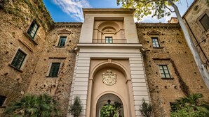Um edifício histórico com um arco central, paredes de pedra e plantas em vasos.