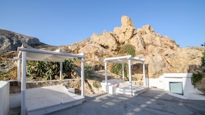 Terraço no telhado com mobiliário externo branco e vista para montanhas rochosas.