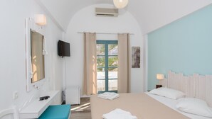 Quarto de hotel com cama, escrivaninha, cadeira, televisão e janela com cortinas.