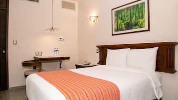 Quarto de hotel com uma cama grande, uma escrivaninha com telefone, uma cadeira, uma luminária na parede e um quadro de uma floresta.