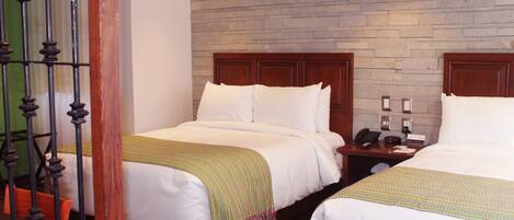 Quarto de hotel com duas camas, cabeceira de madeira, parede de tijolos e uma pequena mesa de cabeceira com telefone e abajur.