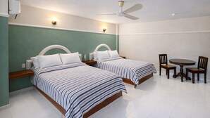 Quarto de hotel com duas camas, um ventilador de teto, uma mesa redonda pequena com cadeiras e um ar condicionado fixado na parede.