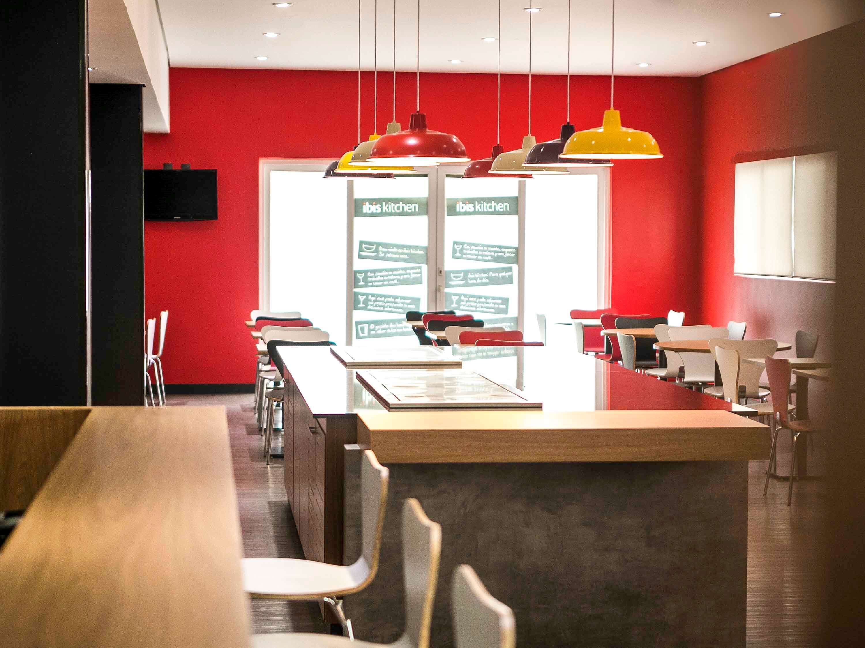 Interior moderno de restaurante com paredes vermelhas, várias mesas de jantar e luminárias pendentes.