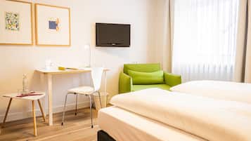 Quarto de hotel com cama, escrivaninha, cadeira, televisão e obras de arte na parede.