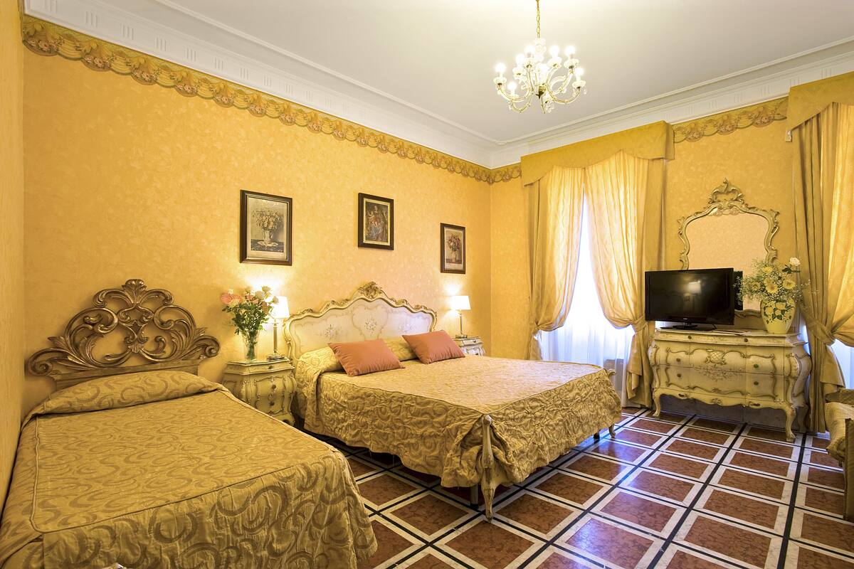 Quarto de hotel com duas camas, uma televisão, cômoda e um lustre.